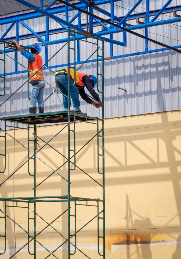 2 construction workers installing high scaffolding for construction of ...
