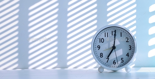 Sunlight and shadow on surface of white round table clock on white desk ...