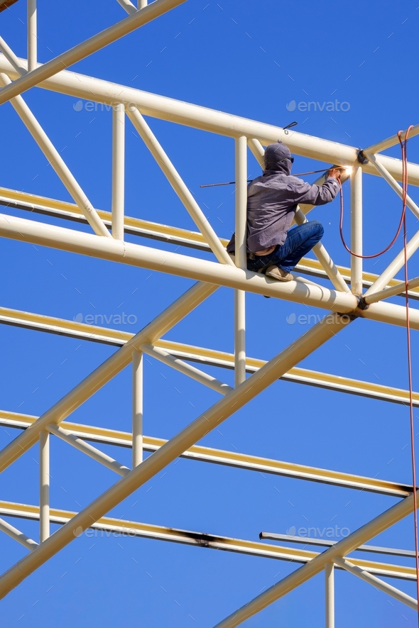 construction worker is welding metal on building roof structure against ...