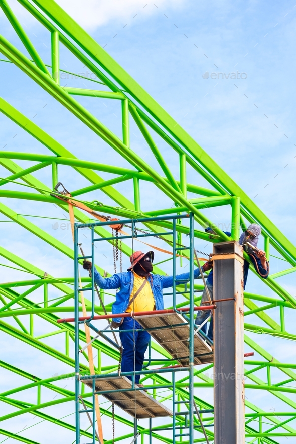 Foreman and construction worker on scaffolding welding metal roof ...