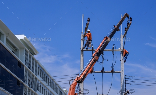 Two electricians with crane truck installing electrical transmission on electric power poles ...