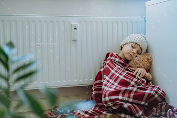 cute little boy wrapped id plaid wearing knit hat sitting by heater ...
