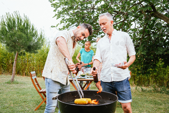 Two men cooking and toasting beers on a barbeque in countryside. At ...