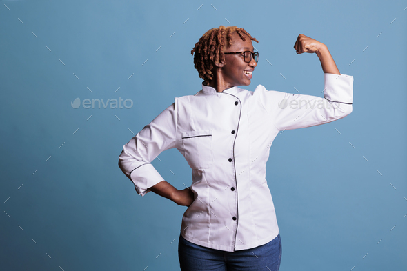 Female chef smiling as looks at arm muscles Stock Photo by DC_Studio
