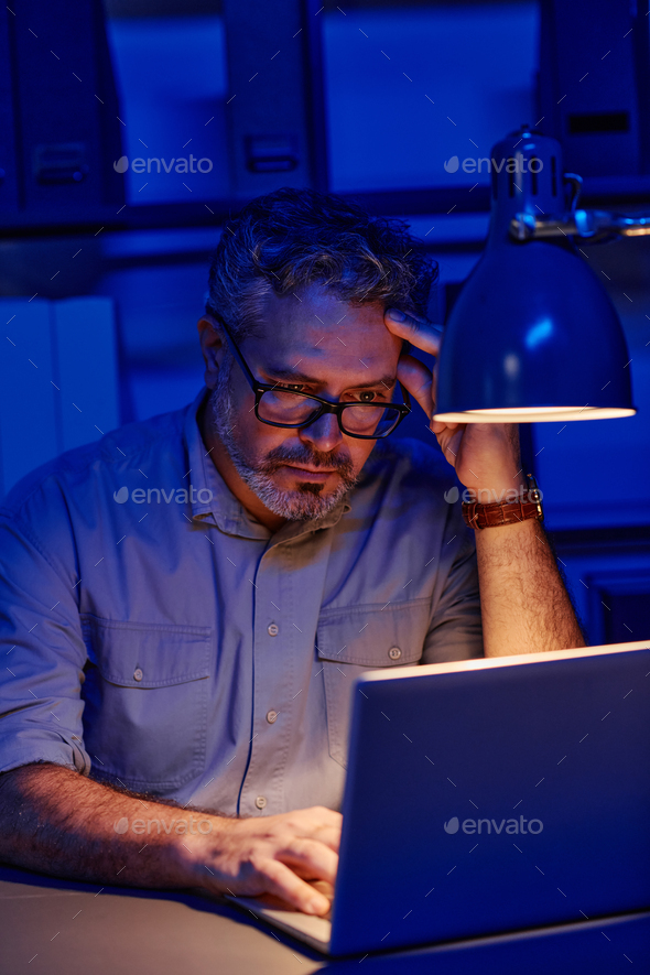 Tired mature male programmer sitting by workplace in front of laptop ...