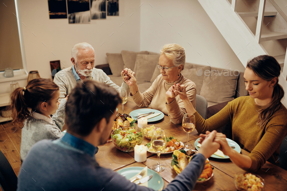 Extended family holding hands and saying grace at dining table. Stock ...