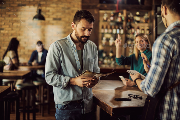 Young man reading menu while making order in a pub. Stock Photo by ...