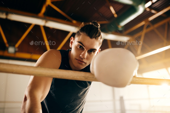 Young male fighter leaning on ropes in boxing ring and looking at ...