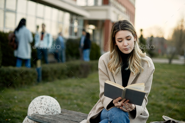 Female university student reading book while relaxing outdoors at ...