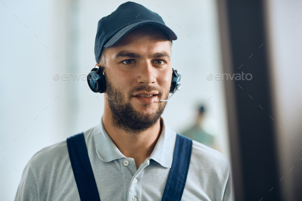 Young mechanic wearing headset while talking to a customer and using ...
