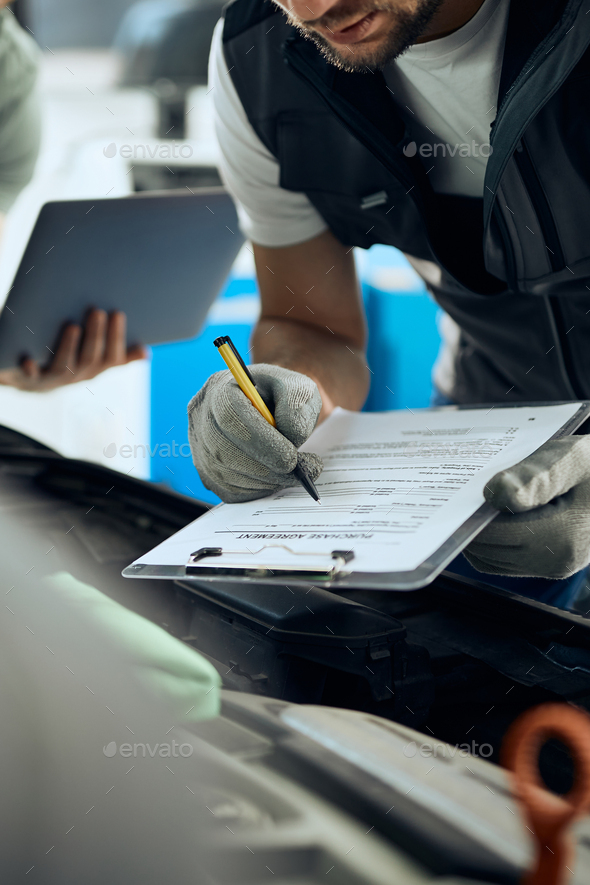 Close up of mechanic taking notes while analyzing car engine with his ...