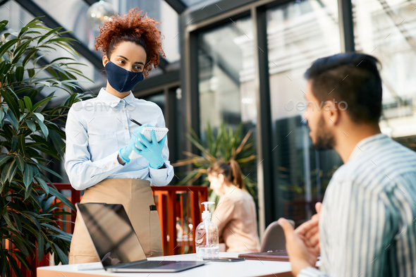 Waitress with face mask talking to guest while taking order from him in ...