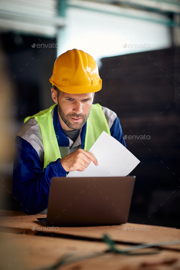 Manual worker using laptop while working at distribution warehouse ...