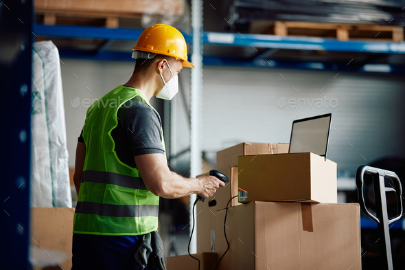 Male worker scanning boxes while using laptop and working in warehouse ...