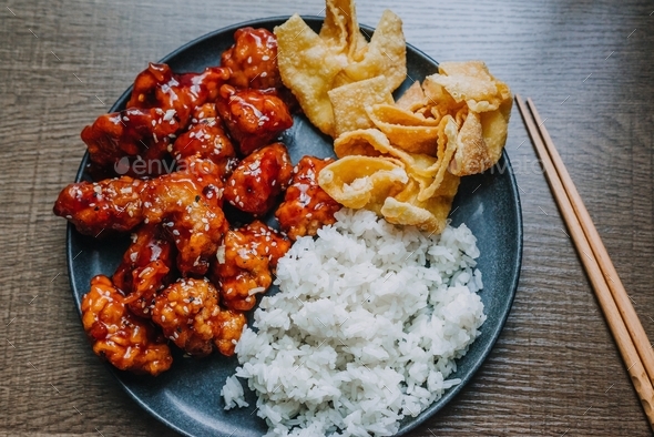 General tsos chicken with white rice and crab rangoon on a dark dish ...