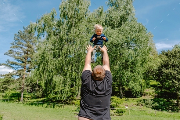 Father throwing little smiling baby child boy into air against green ...