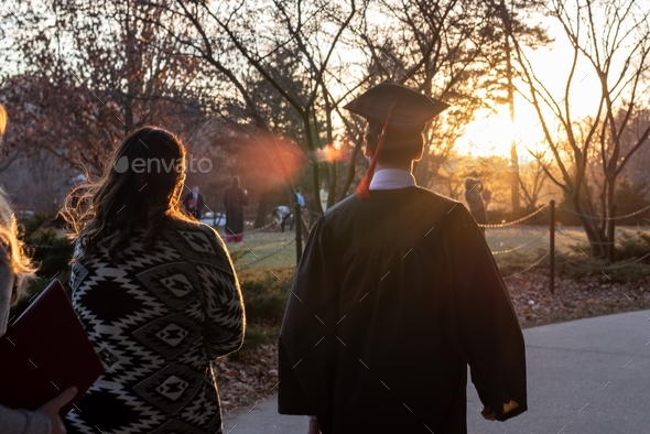 Graduate walking across university campus in cap and gown Stock Photo ...