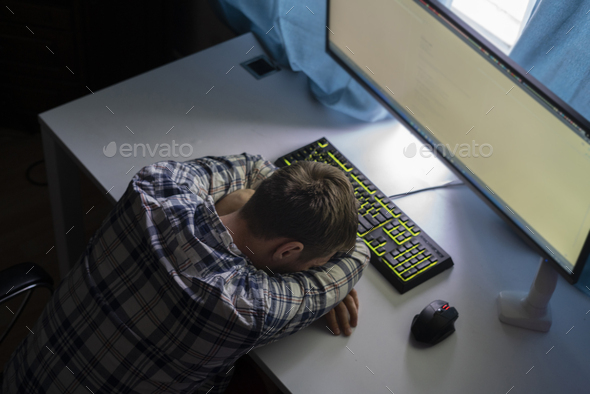 a sick and tired male worker at night doing some work in the office ...