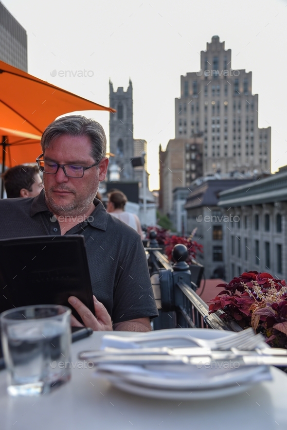 Man ordering from a menu at rooftop restaurant Stock Photo by krisprahl