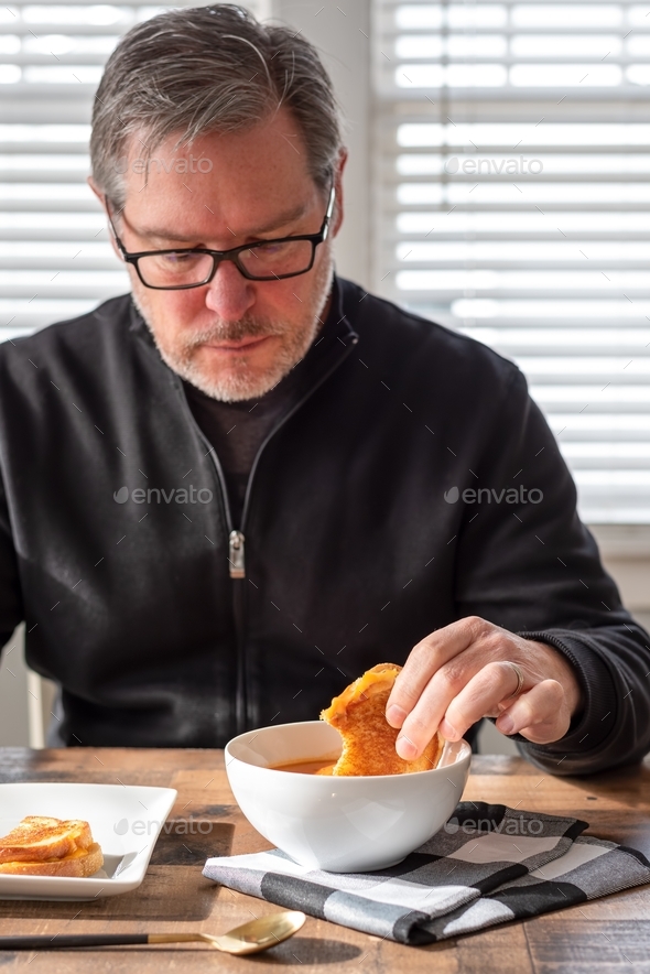 Man dipping a sandwich in a bowl of soup Stock Photo by krisprahl