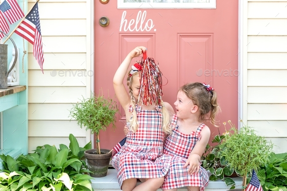 Two happy playful little girls sitting on the back steps on Fourth of ...