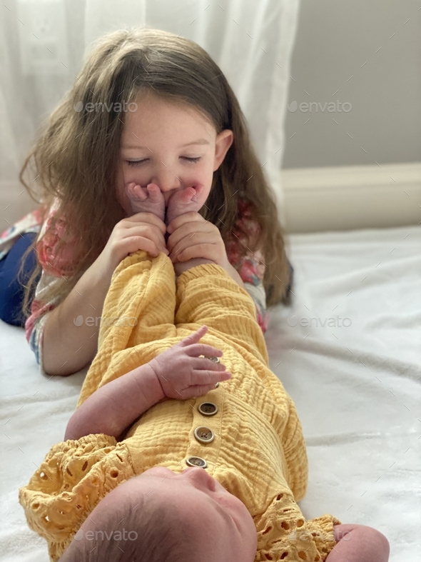 Little girl kissing her new baby sister’s feet Stock Photo by krisprahl