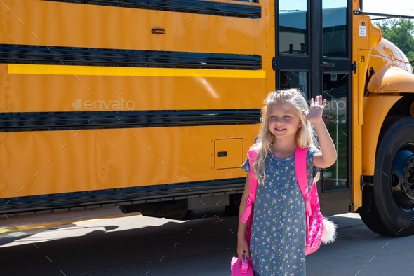 Little girl waving good-bye as she waits to get on the school bus Stock ...