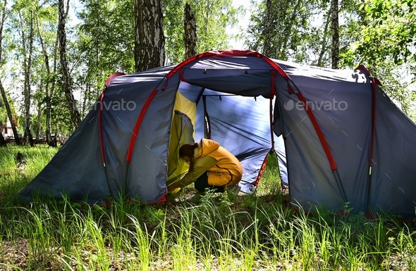 a girl in a yellow raincoat sets up a blue tent for camping in the ...
