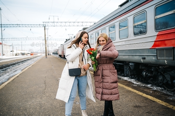 two girls at the train station look at the clock, talk on the phone, meet with flowers Stock ...