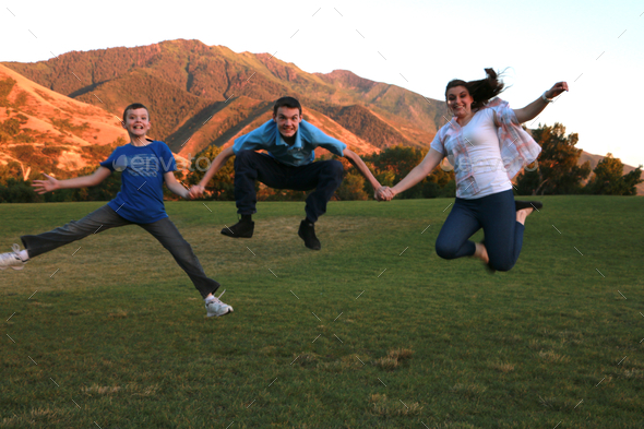 Action capture of three siblings holding hands jumping in the air with ...