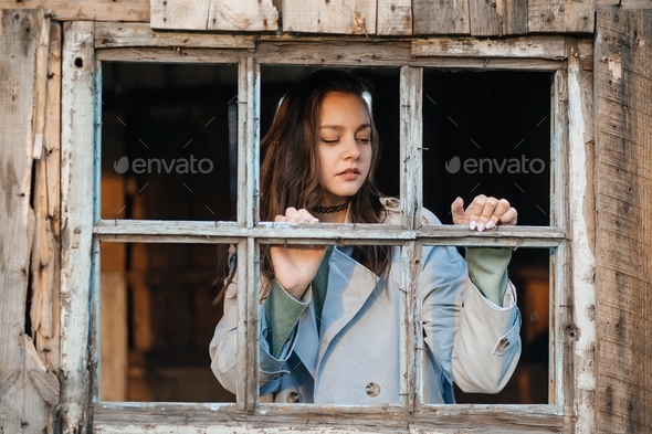 girl looks out the window from an old wooden house Stock Photo by ...