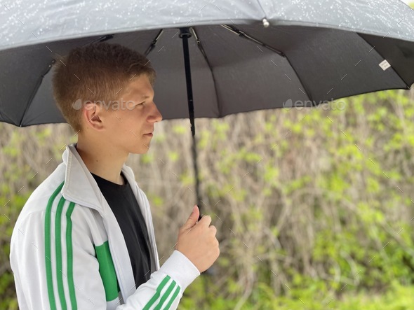 A young man goes in light rain under an umbrella Stock Photo by keshakesha