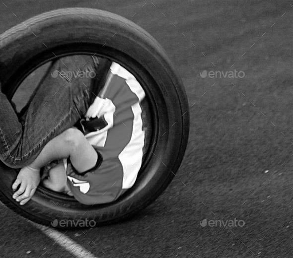Monochromatic image of adolescent boy curled up in a tire rolling ...