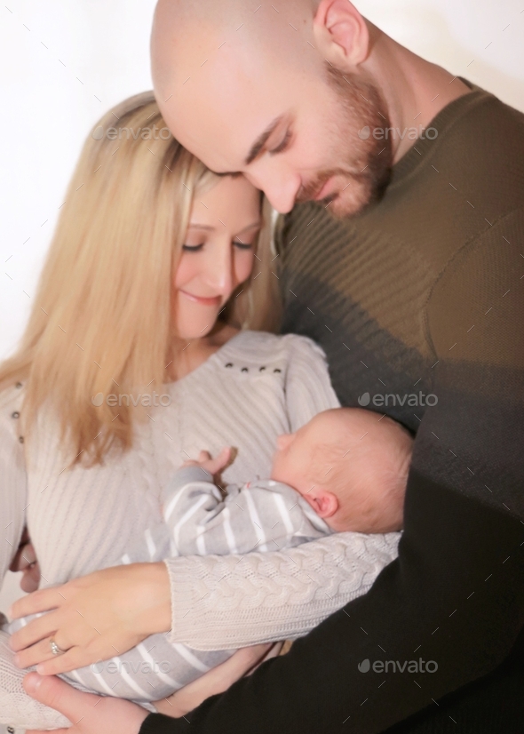 Vertical portrait of new parents wearing neutral colors holding their ...