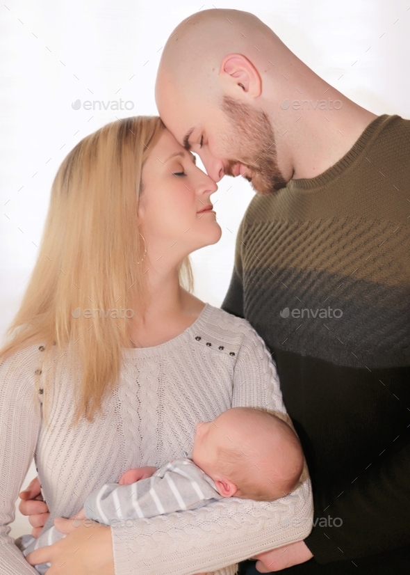 Vertical portrait of new parents wearing neutral colors holding their ...