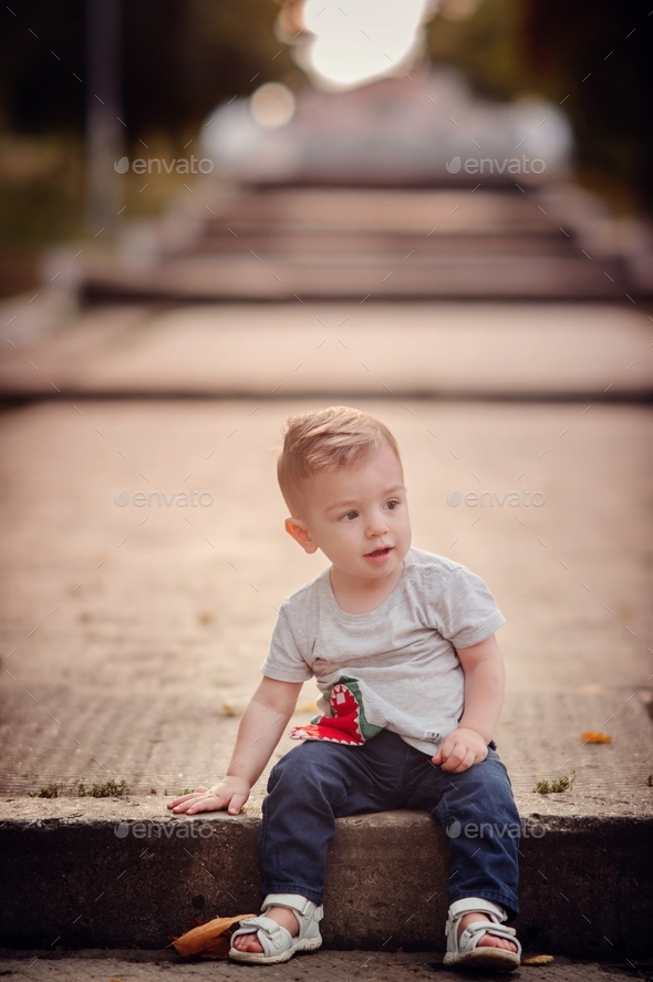 Little happy boy sitting on big stairs in park Stock Photo by iviphoto93