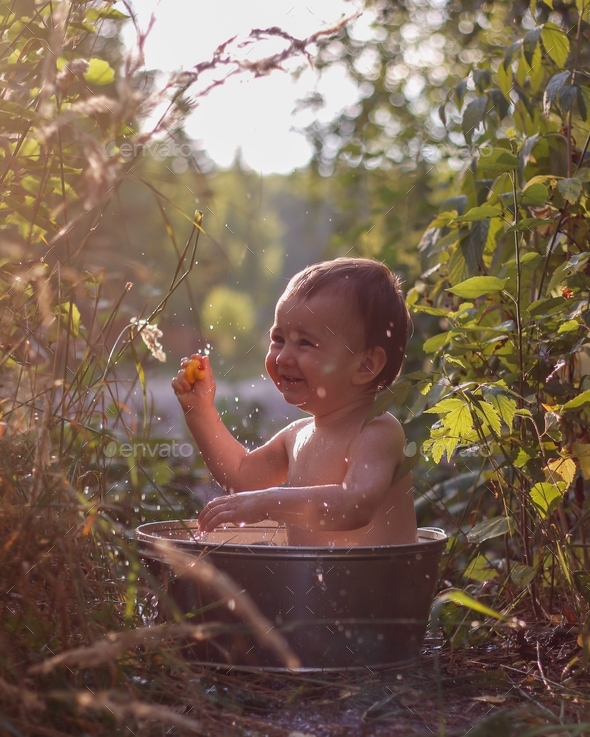 Happy child bathes in a basin outdoors in summer. Stock Photo by ElenNika