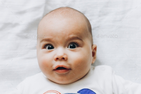 Chubby Cheeky Baby with big eyes on the bed. Happy smiling baby boy ...