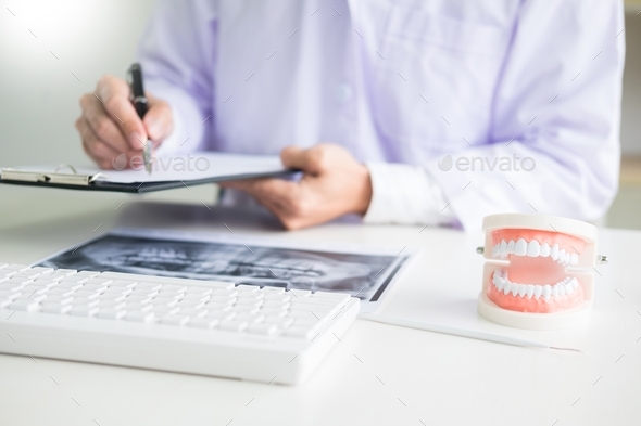 Concentrated dentist sitting at table with jaw samples tooth model in ...