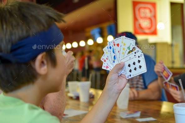 Child playing cards with his family at a restaurant table Stock Photo ...