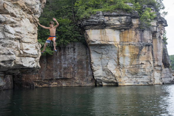 Boy jumping off rock wall into a lake Stock Photo by shannonfieldsphoto