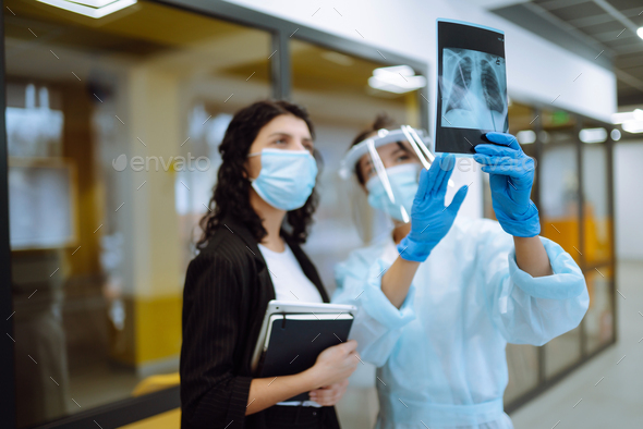 A female doctor in visor and protective gloves discussing an x-ray ...