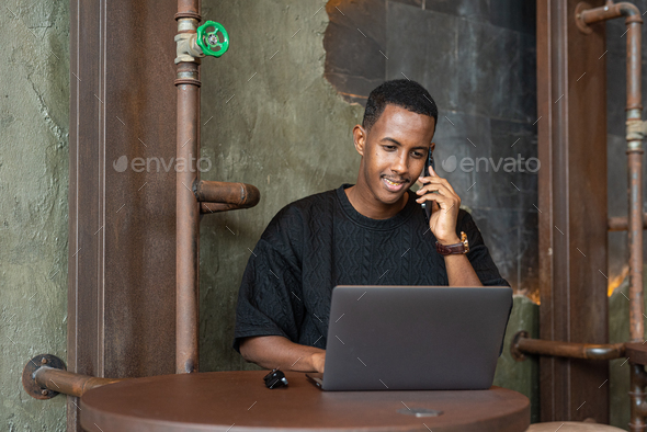 Handsome black man sitting and using laptop computer indoors Stock ...