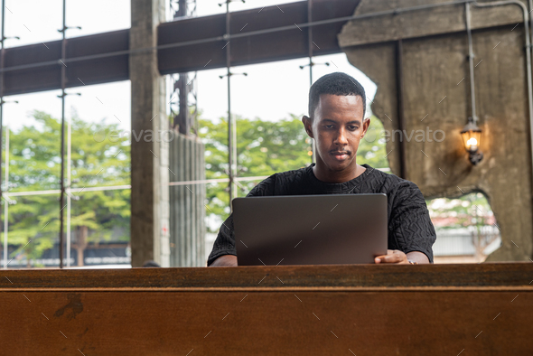 Handsome black man sitting and using laptop computer indoors Stock ...