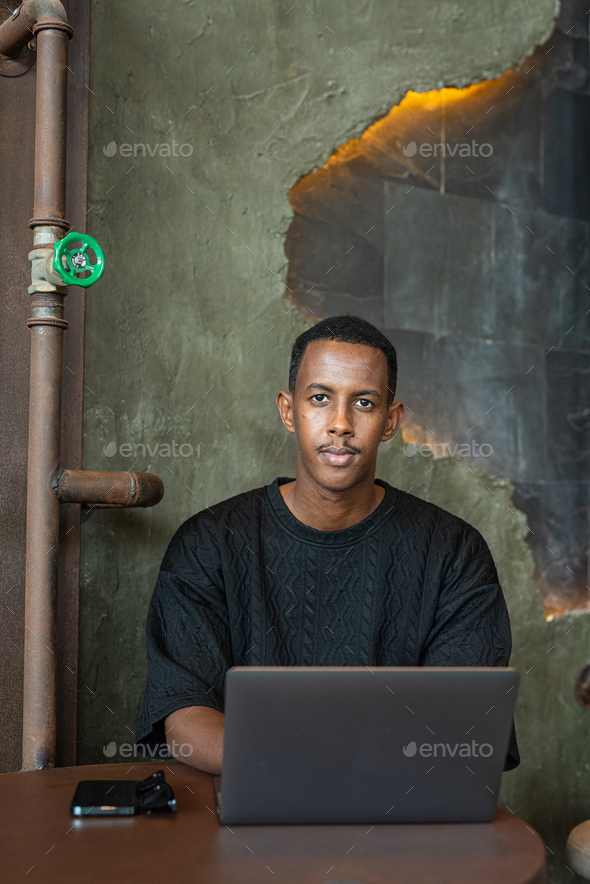Handsome black man sitting and using laptop computer indoors Stock ...