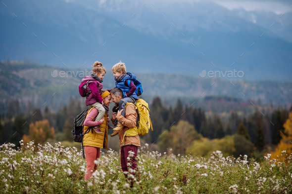 Happy parents with their little kids on piggyback at autumn walk, in ...