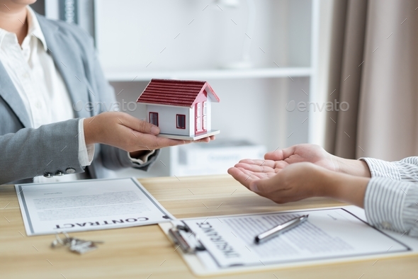 Insurance concept the estate agent holding a house model and giving it ...