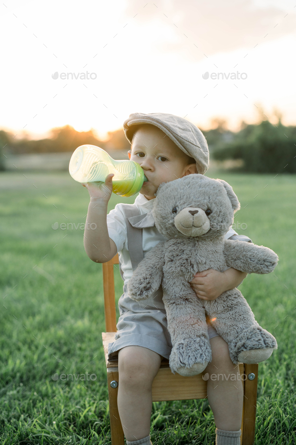 Little boy drinking out of his sippy cup and holding his teddy bear ...