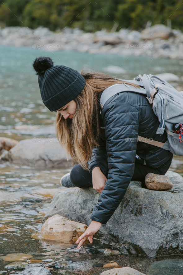 Girl sitting on a rock in a lake picking up rocks Stock Photo by takemewu31