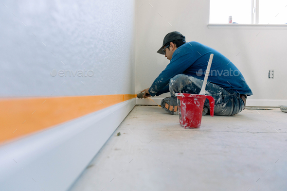 Man taping the wall to paint the trim white on a home renovation ...